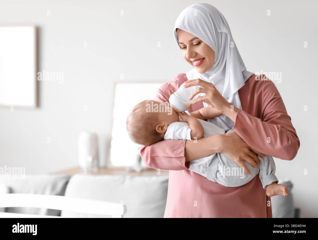 Happy Muslim mother in hijab feeding her cute little baby with milk ...