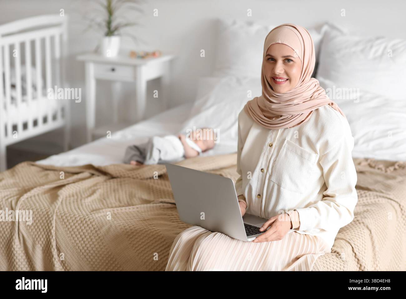 Happy Muslim mother in hijab using laptop while her cute little baby ...