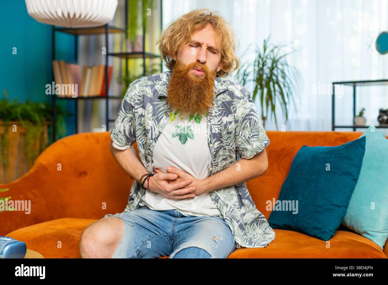 Caucasian redhead man sitting on sofa feeling sudden strong abdominal ...