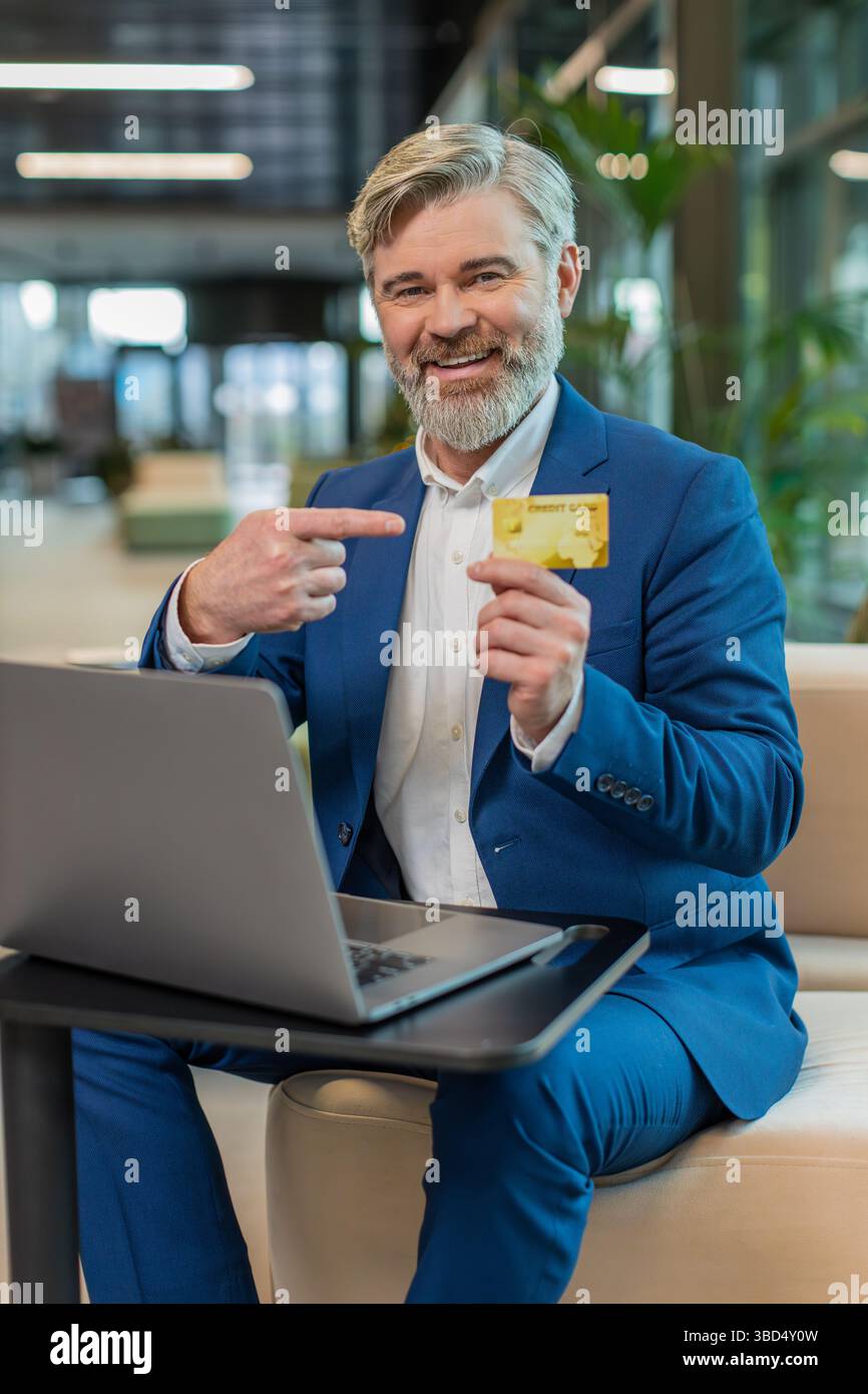 Smiling mature businessman using bank credit card and laptop for online ...