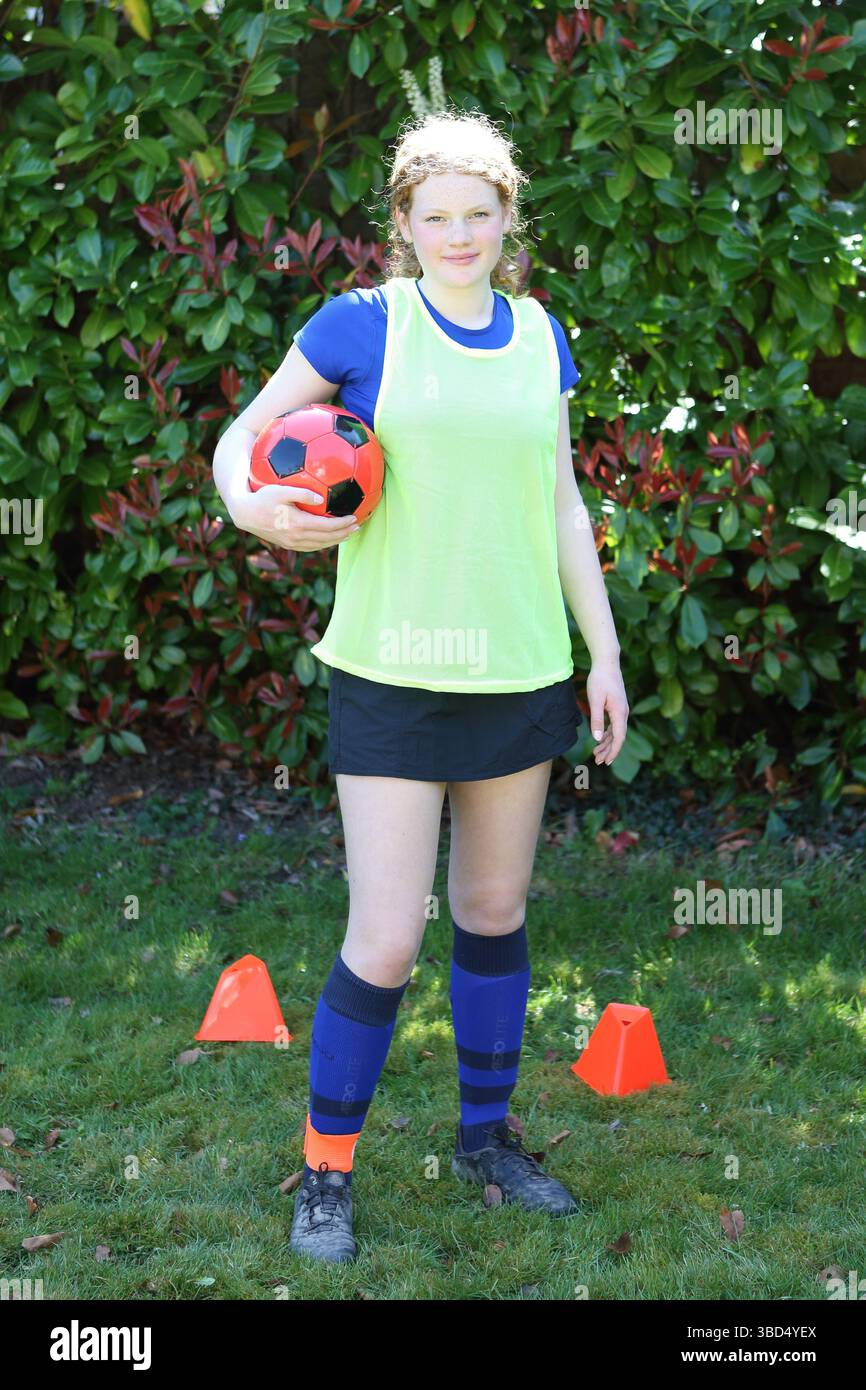 Girl footballer holding ball under arm wearing yellow bib over blue ...