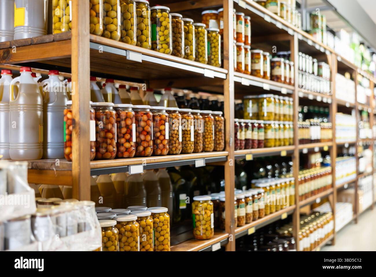 Marinated whole unpitted green olives in jars on shelf rack in store ...