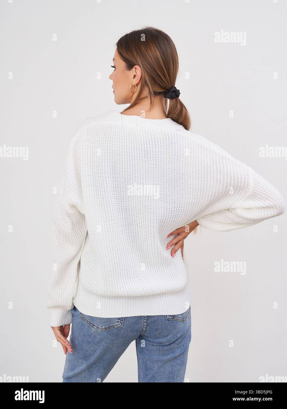 Young woman with brown hair in a ponytail wearing a white knit sweater ...