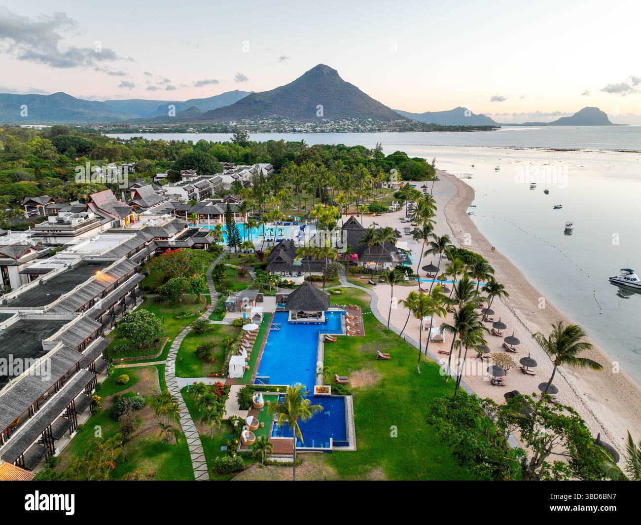 Aerial view of beachfront resort pool framed by palm trees and mountain ...