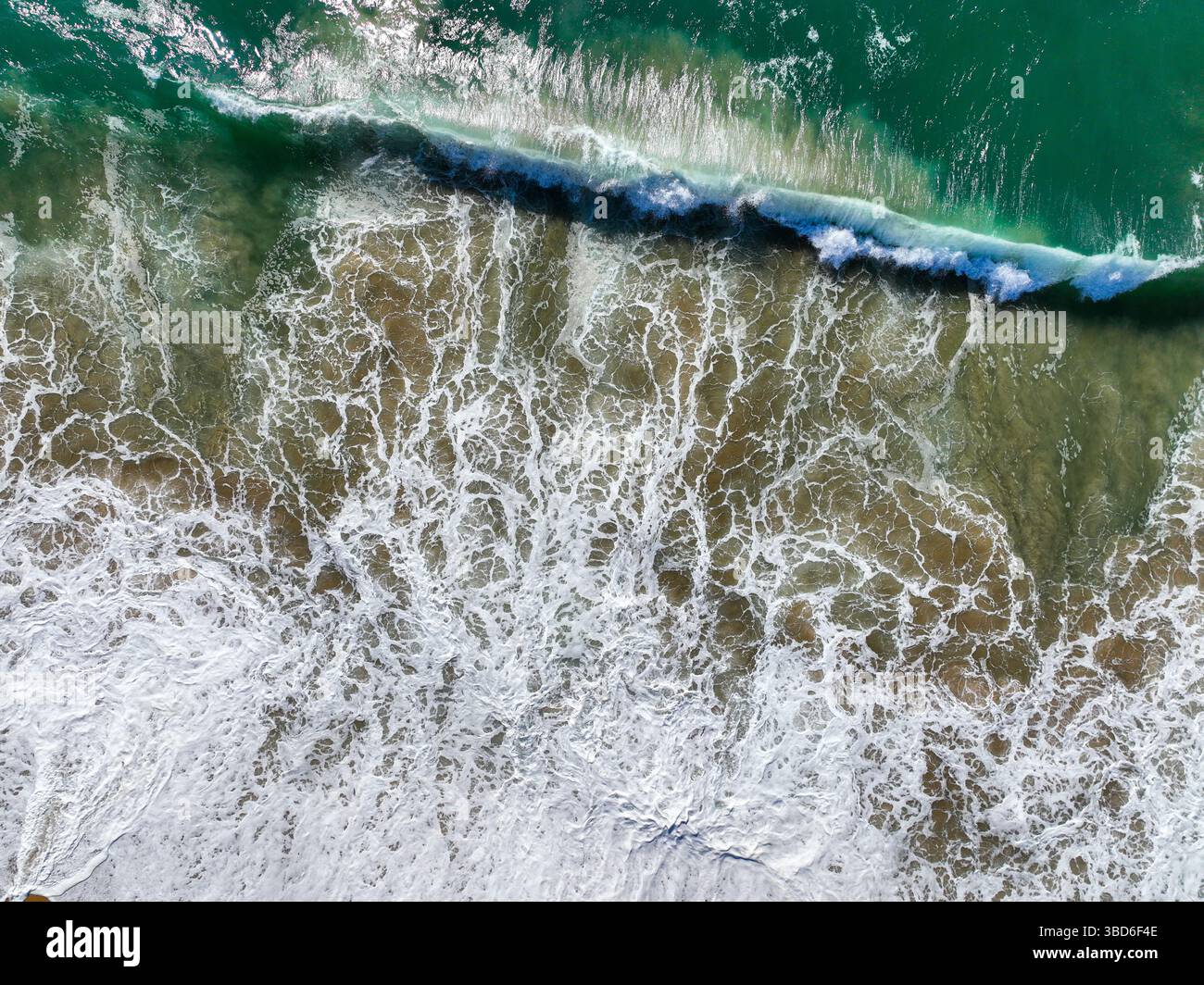 Drone photo showing ocean waves hitting a beach and forming foamy ...