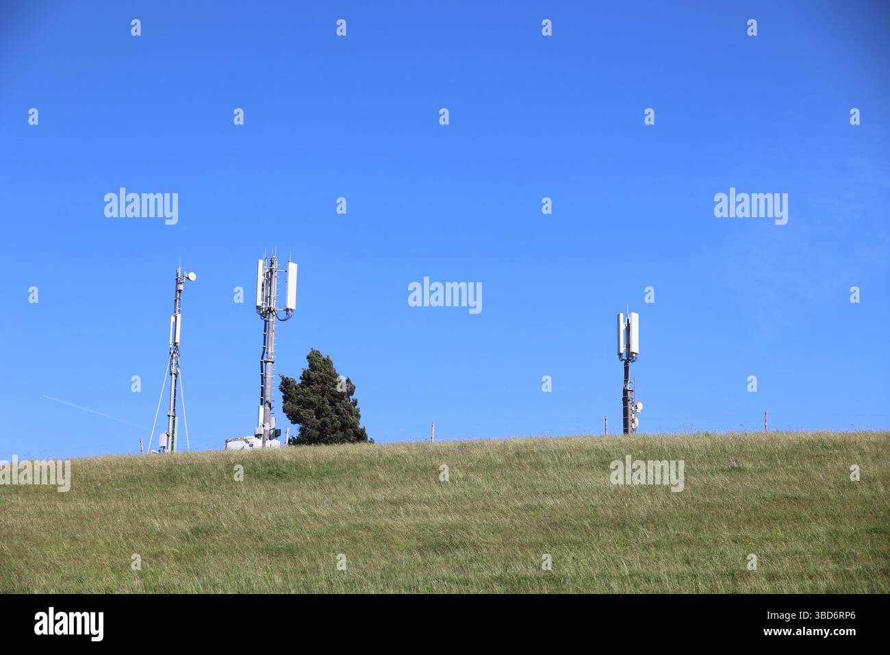 Three tall towers with antennas on top of them are standing in a grassy ...