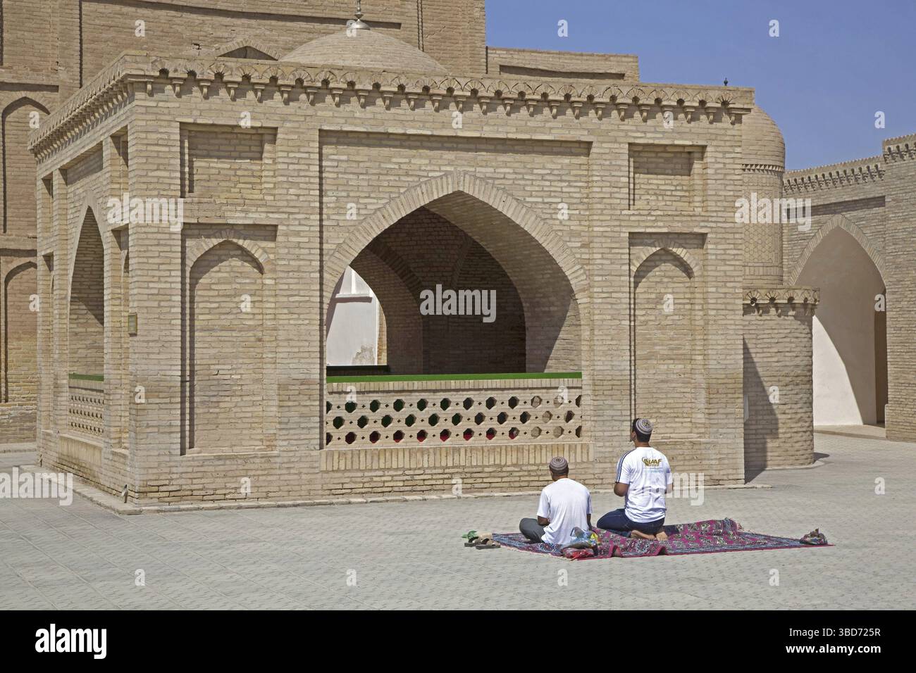 Two Turkmen praying on carpet in front of Mausoleum of Hoja Yusuf ...