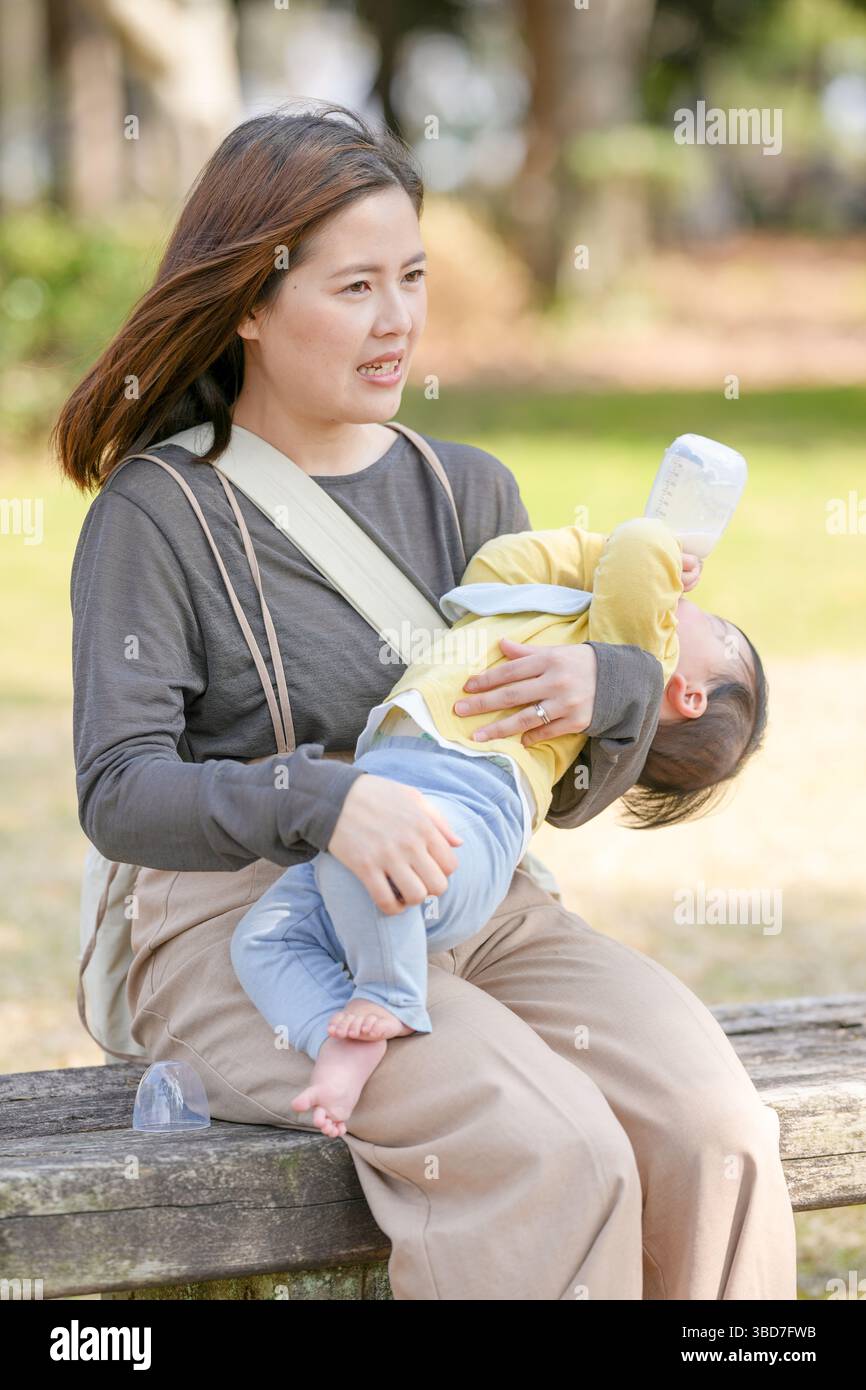 In March, at a sunny forested park in Japan, a Japanese mom in her thirties sits on a bench and ...
