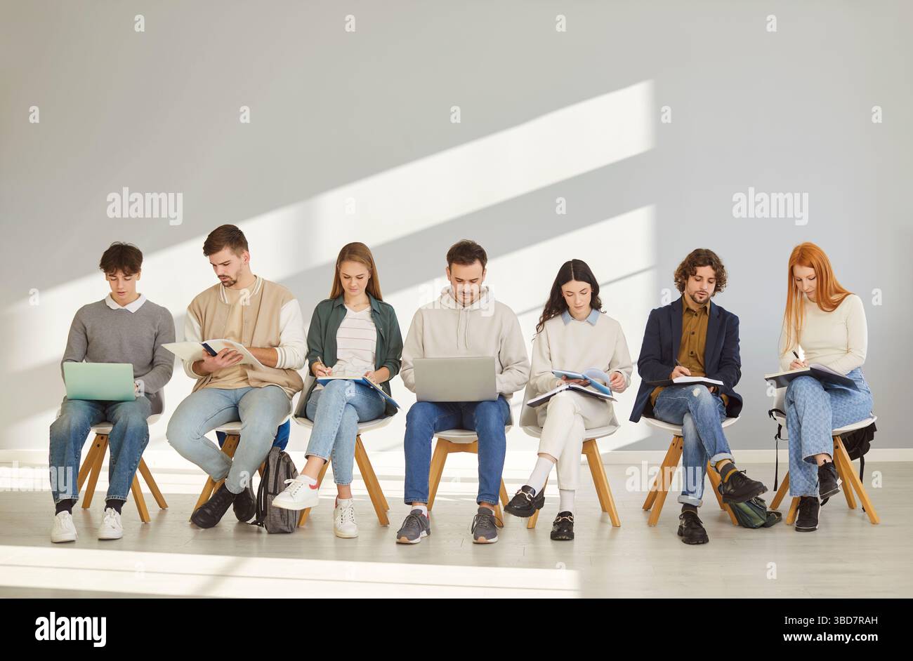 Focused young students or job seekers sitting in row, reading books ...