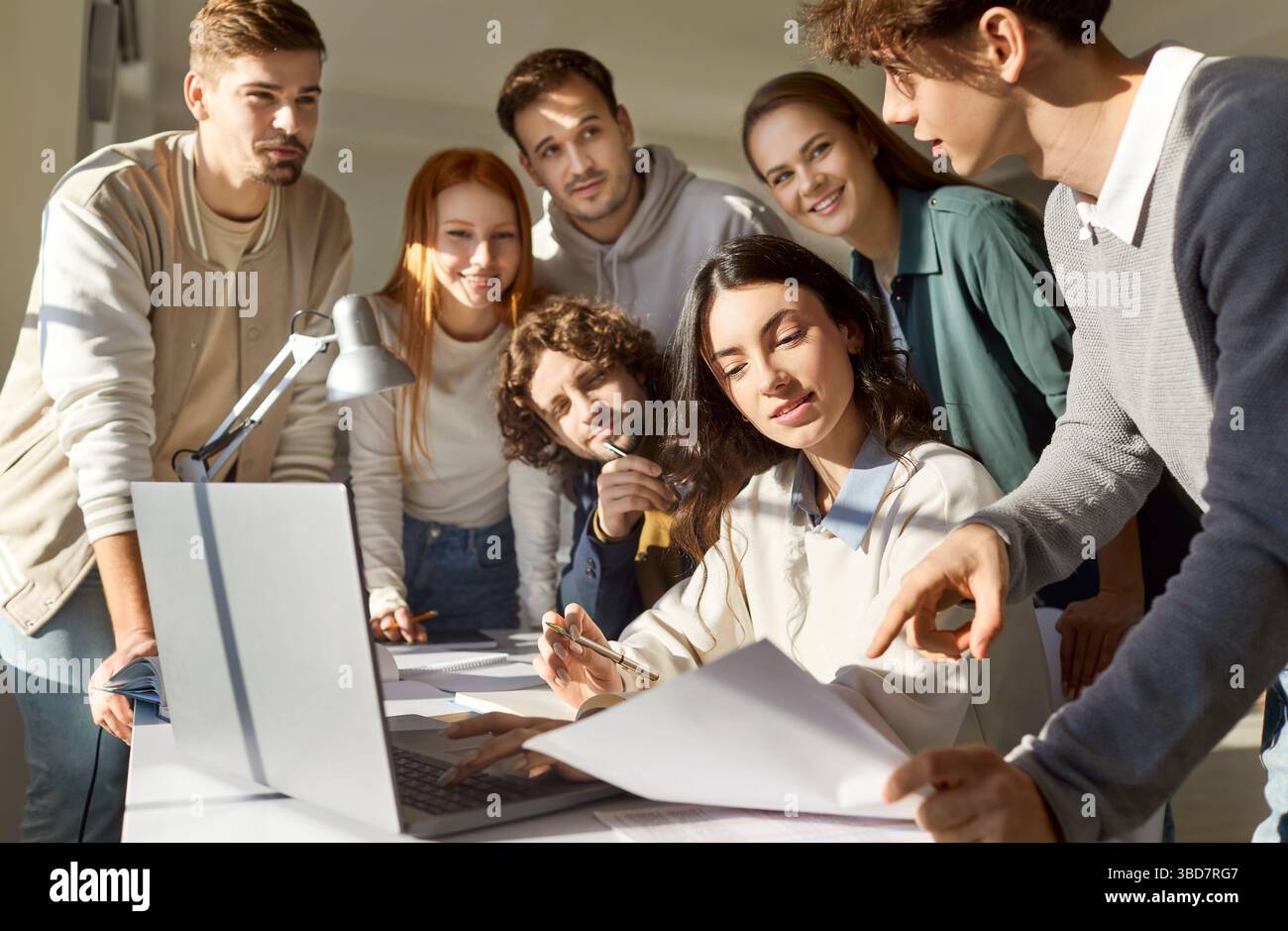 University students gathered around desk discussing project and sharing ...