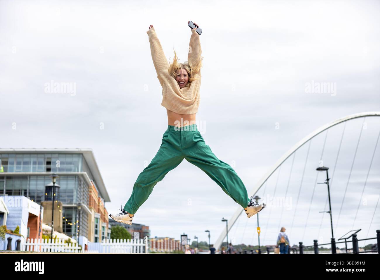 Front-view full-length shot of a mid adult woman jumping with her arms ...
