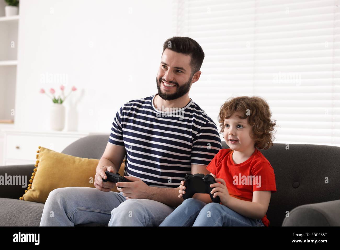 Happy father and his son playing with game controllers together on sofa ...