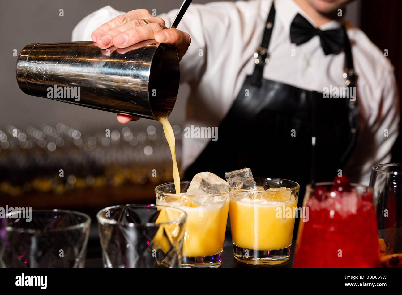 Close-up of bartender in formal attire pouring vibrant orange cocktail ...