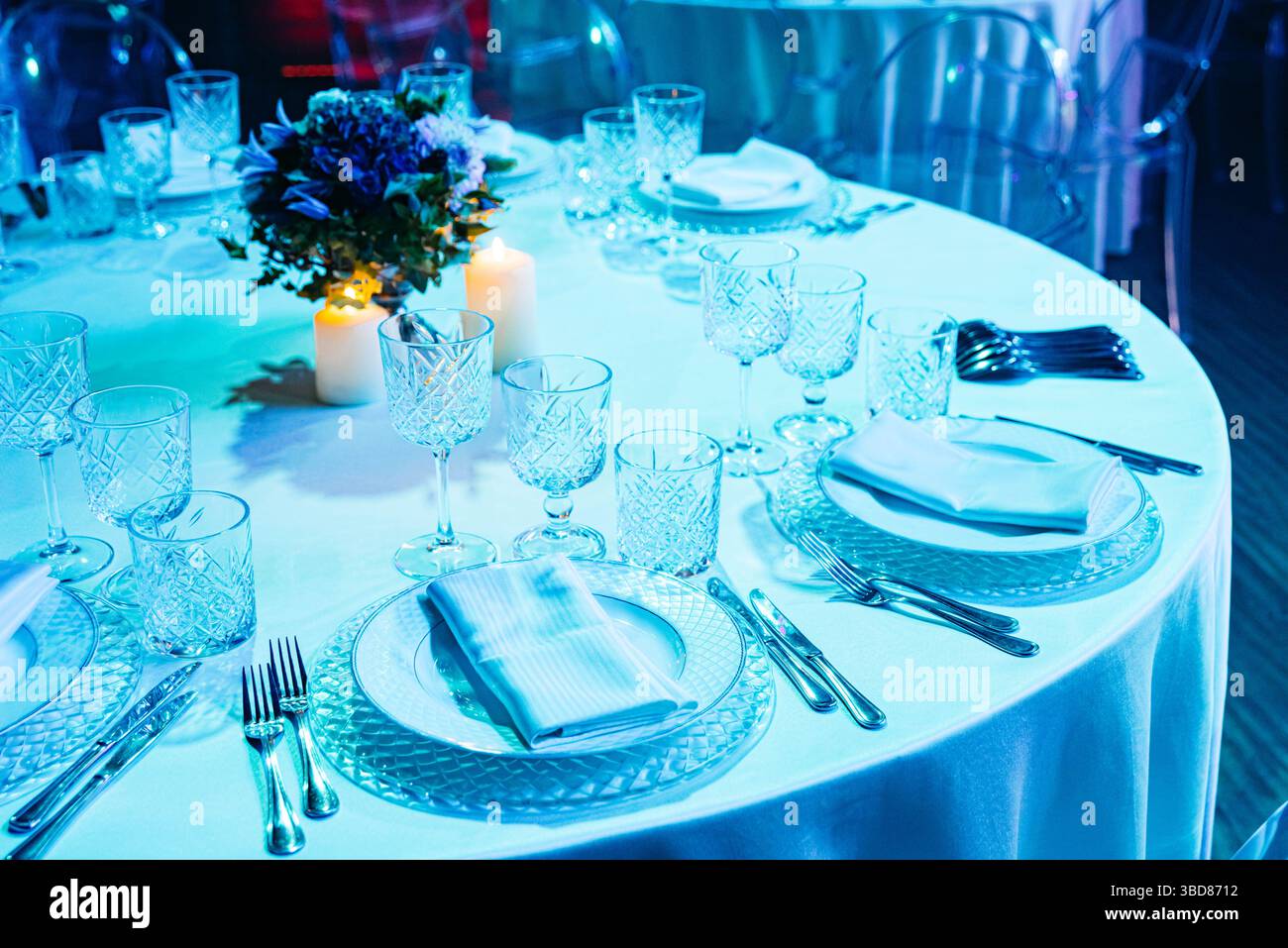 Beautiful round banquet table with crystal glasses, floral centerpiece, and candles, prepared ...