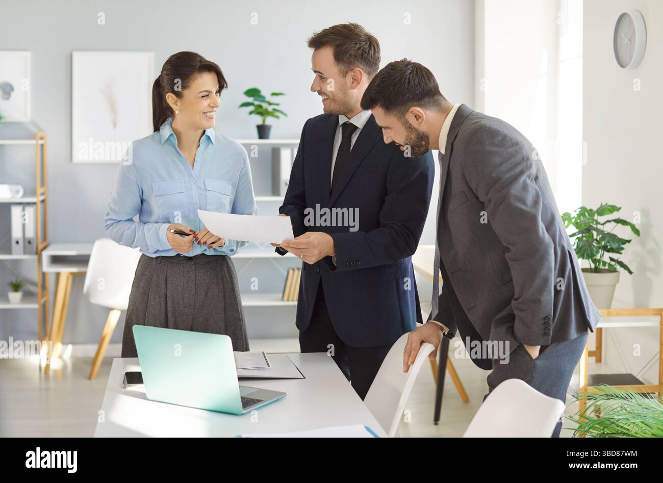 In modern office, three colleagues engage in friendly discussion while ...