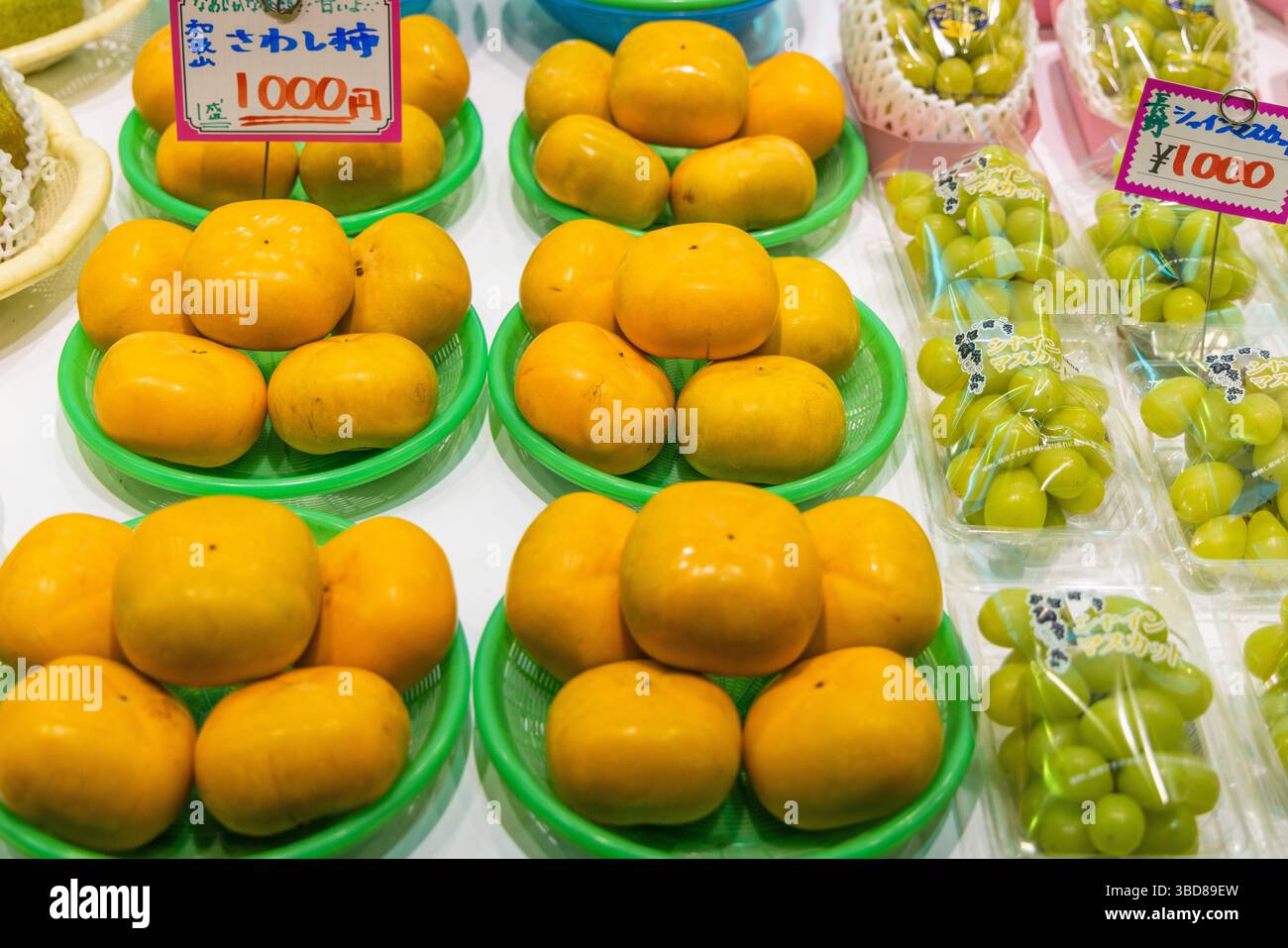 Persimmons and green grapes displayed in plastic trays at a Japanese ...