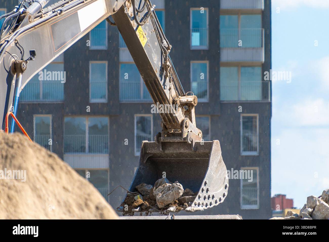 Excavator digging at urban construction site with modern building in ...