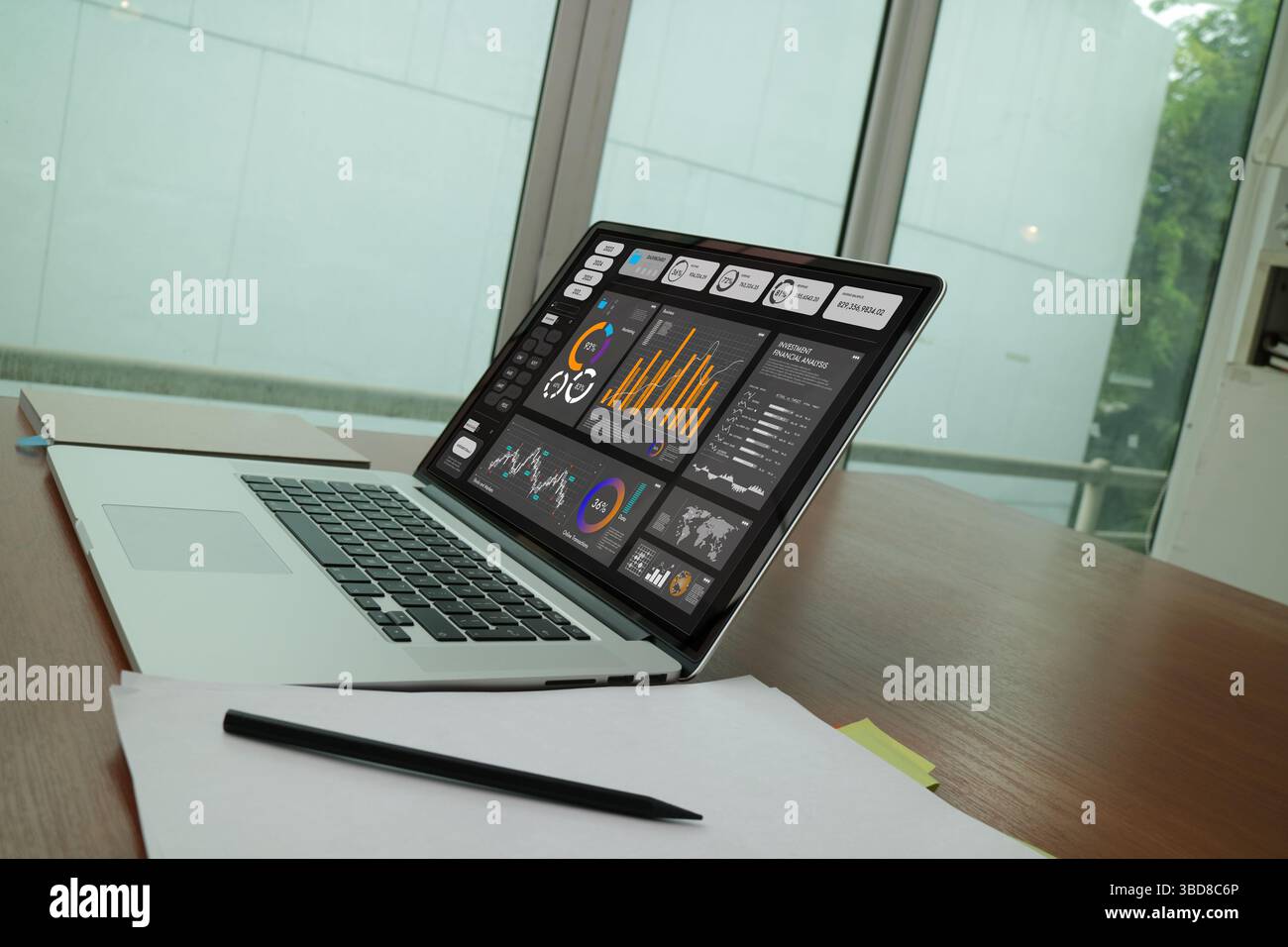 A modern workspace featuring a laptop displaying a financial analytics dashboard with colorful ...