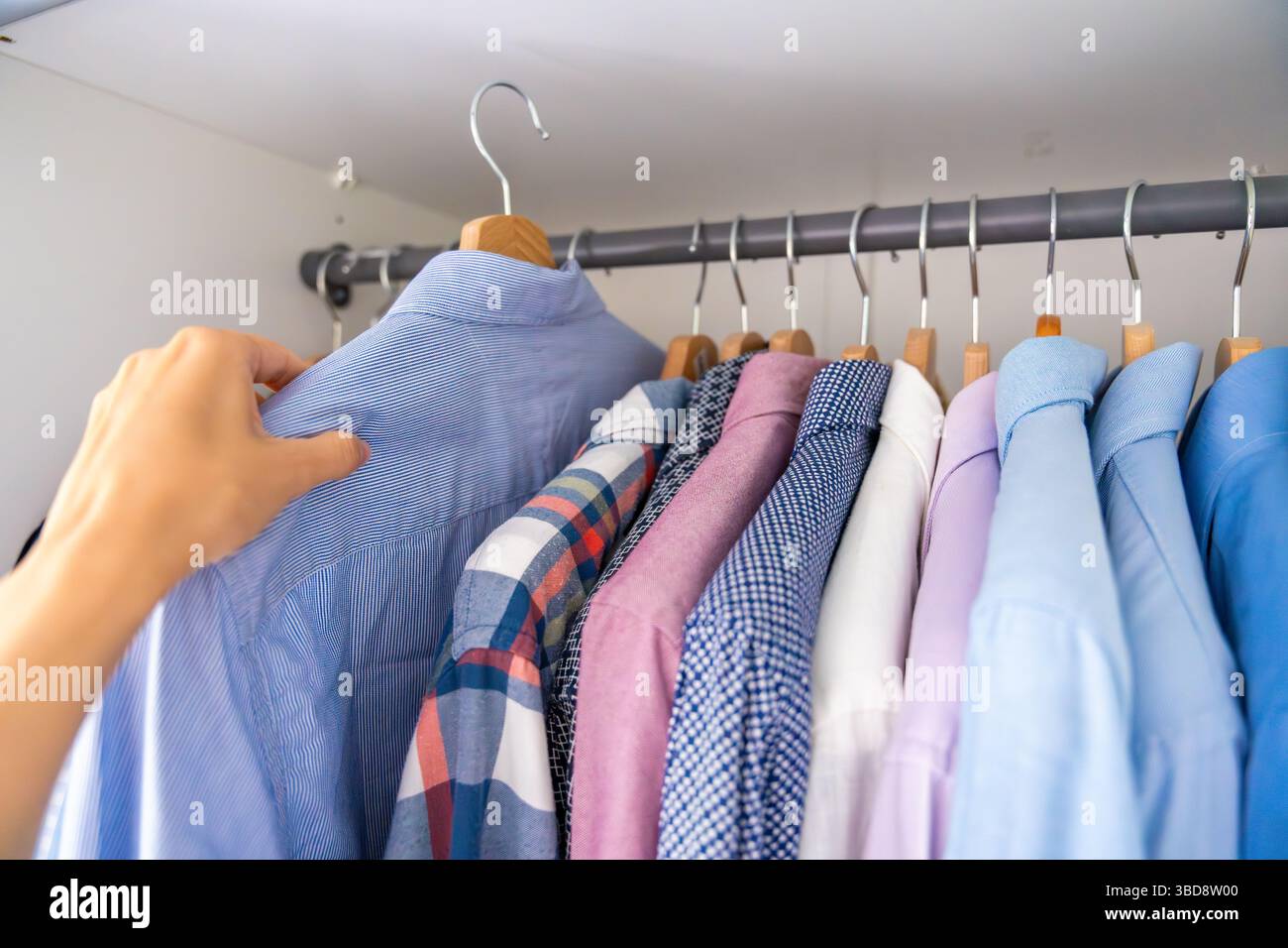 Male hand selecting a shirt from a wardrobe full of clothes on wooden ...