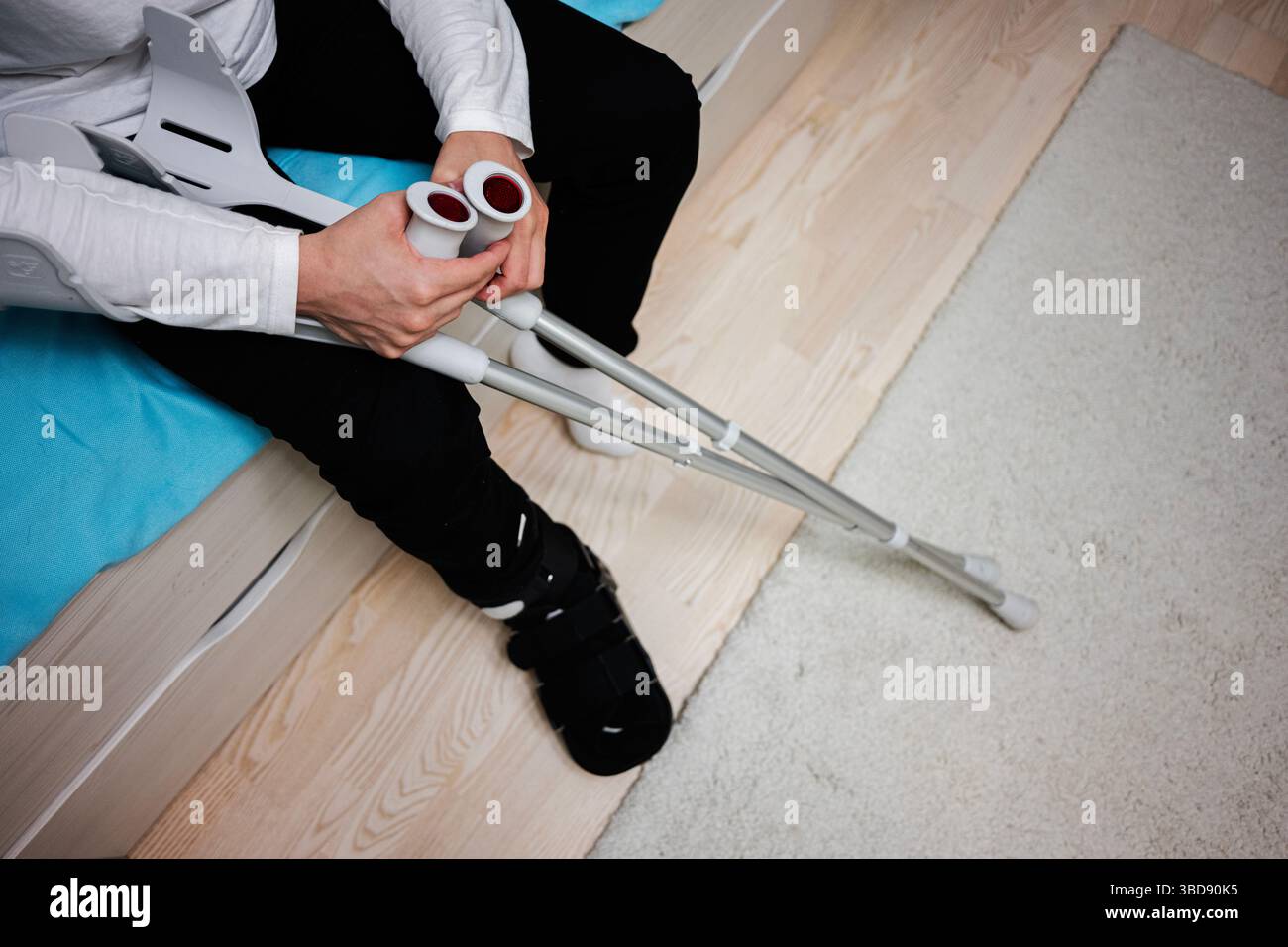 A person seated on a bed holding crutches wearing a black orthopedic ...