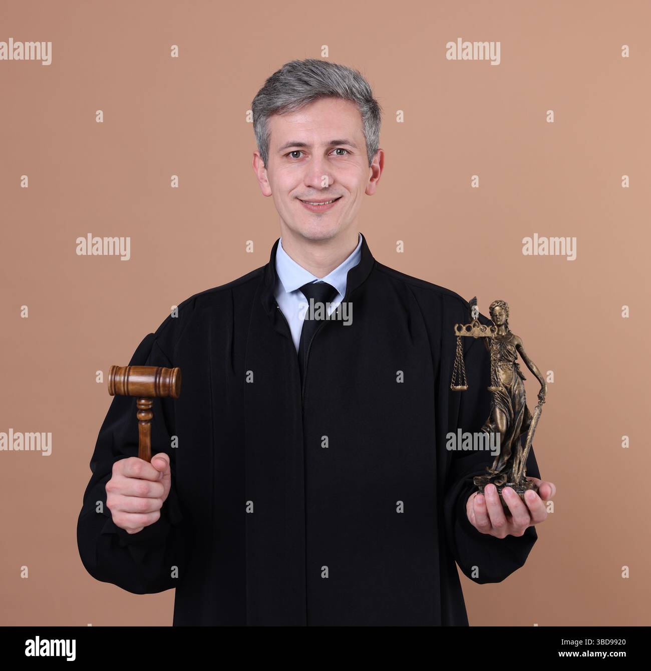 Smiling judge with mallet and statue of Lady Justice on beige ...