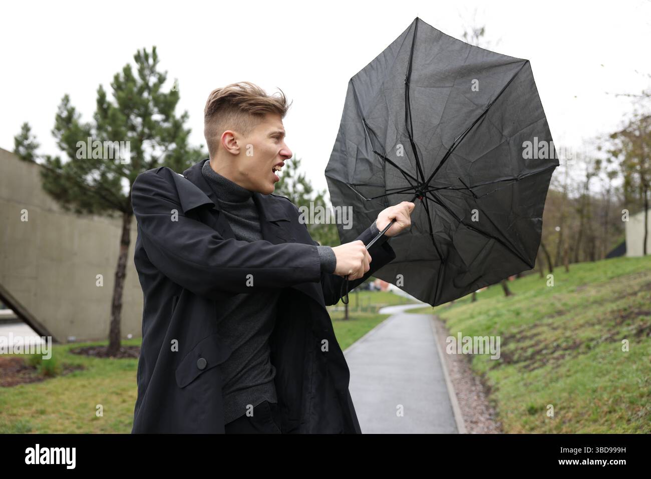 Man with broken umbrella fighting wind under rain outdoors Stock Photo ...