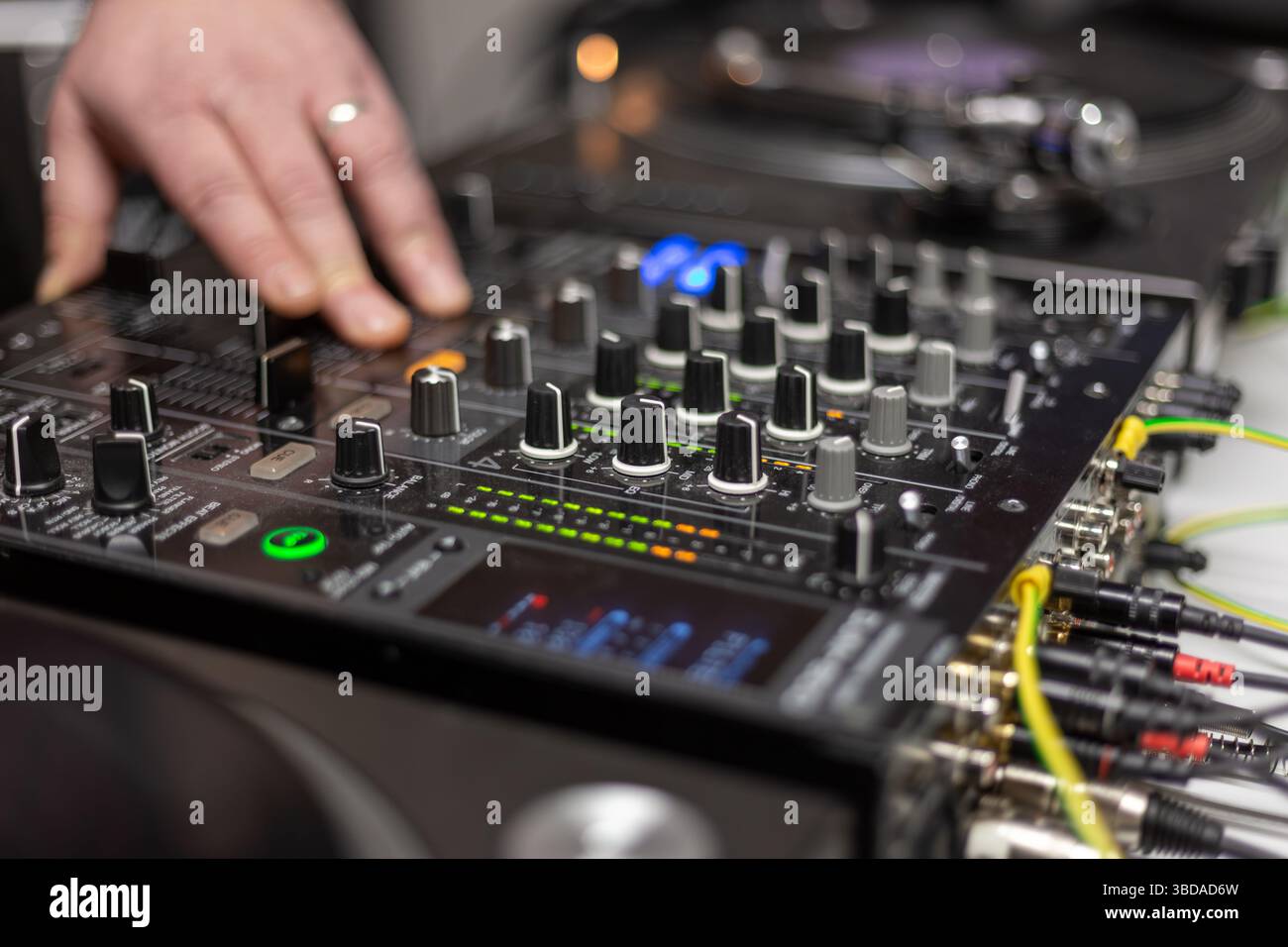 A hand adjusts the mixing console of a DJ setup, with various knobs and ...