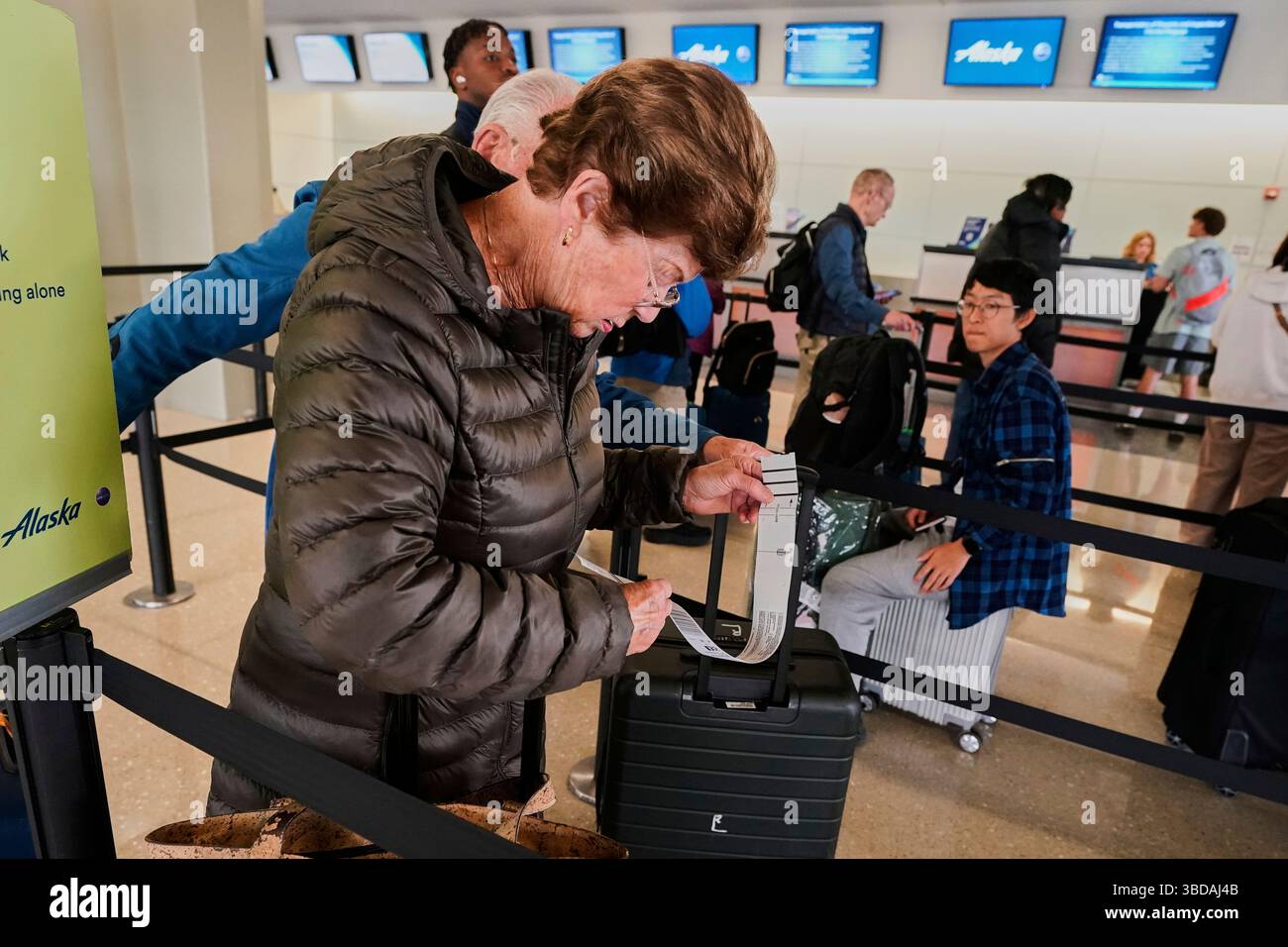A woman checks her baggage tag as she waits in line at the Alaska ...