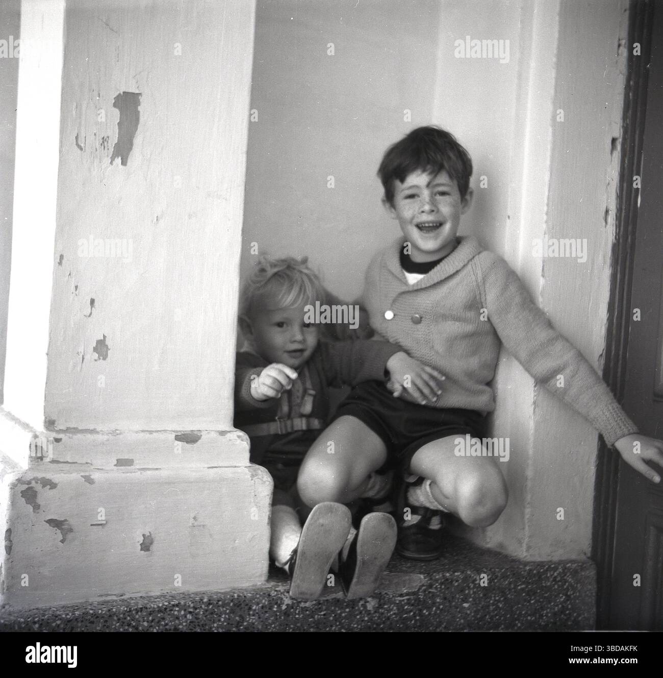 1960s, historical, two young boys playing a game of hide & seek, hiding beside each other in an ...