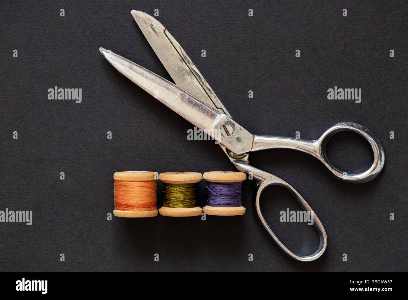Dressmaker scissors and wooden spools of thread on black background ...