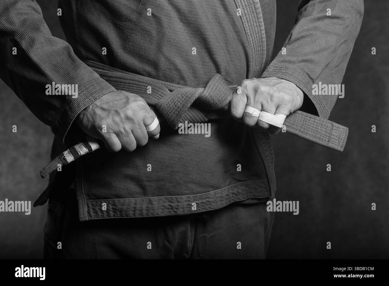 male hands with taped fingers on a tight tied belt on a sports kimono ...
