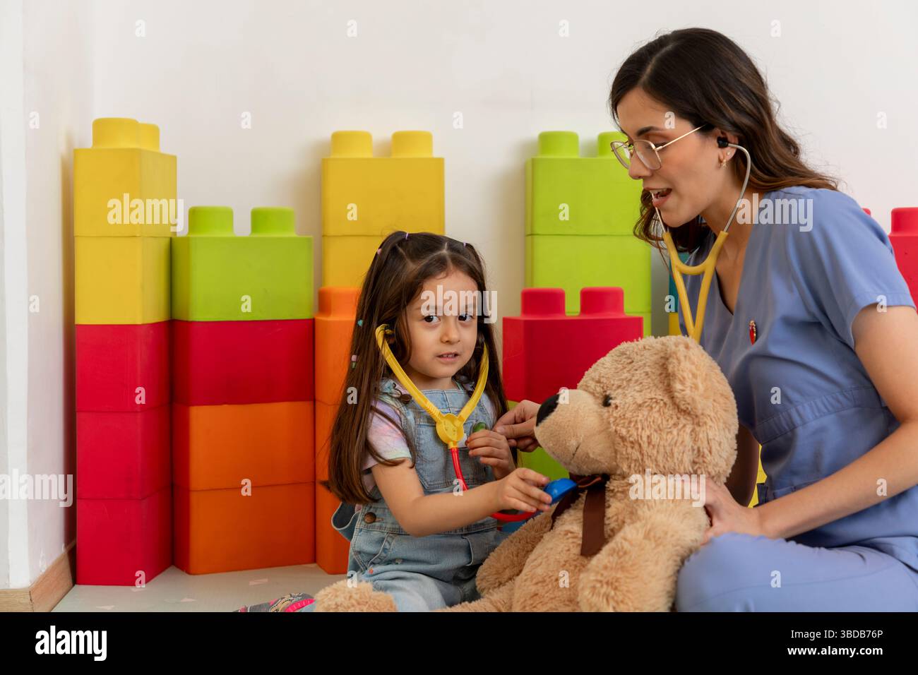 Young female pediatrician helping a little girl using a toy stethoscope ...