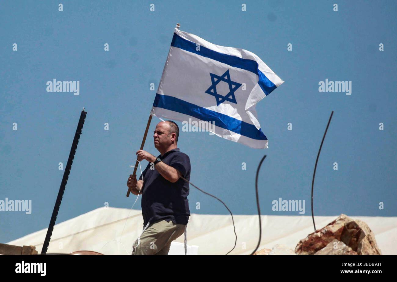 A Jewish settler raises an Israeli flag on Palestinian land near ...