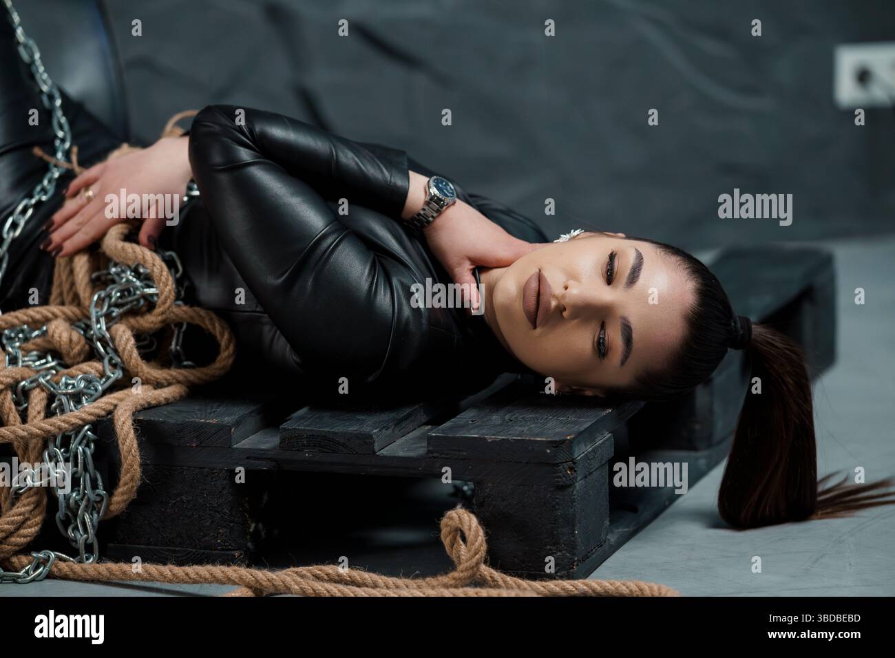 Dramatic image of a young woman bound with chains on a wooden pallet ...