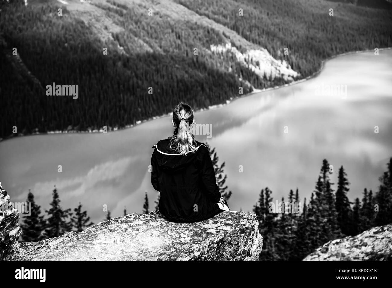 Tourist sitting on a rock ledge overlooking Peyto Lake in Banff ...
