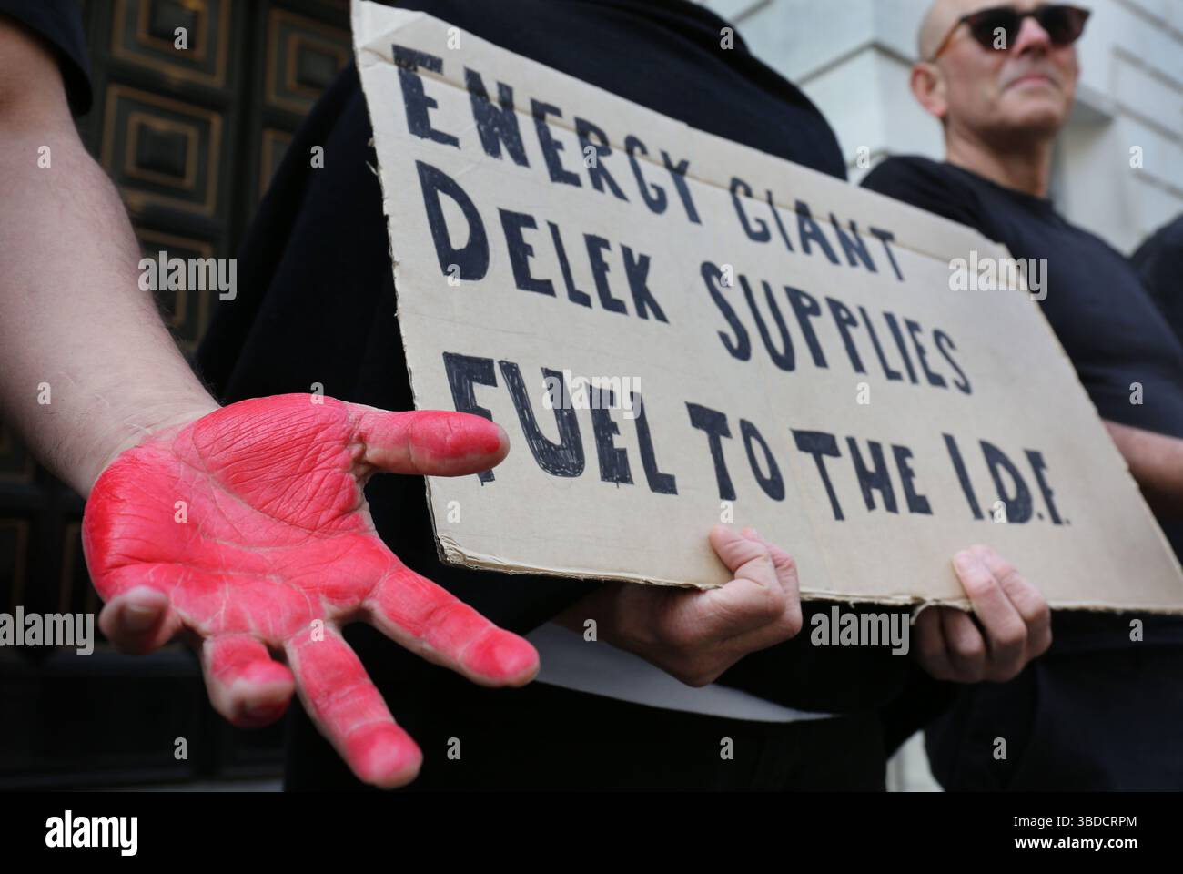 A protester with a red painted hand holds a placard that says ‘Energy ...