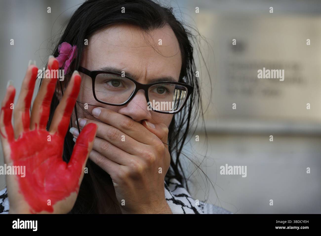 A protester is seen with a red painted hand while he covers his mouth ...