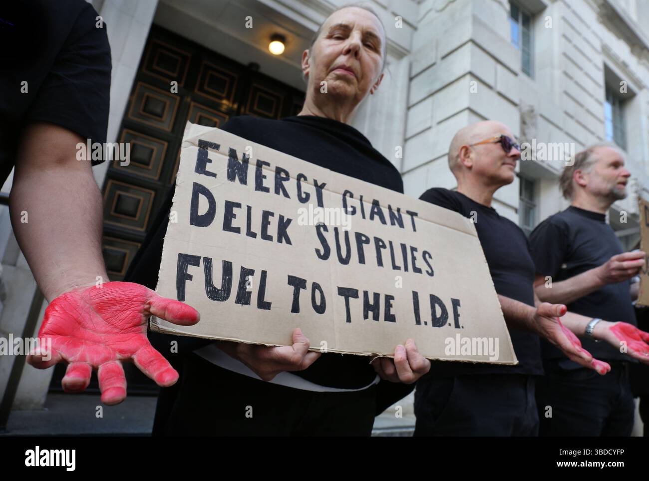 A protester with a red painted hand holds a placard that says ‘Energy ...