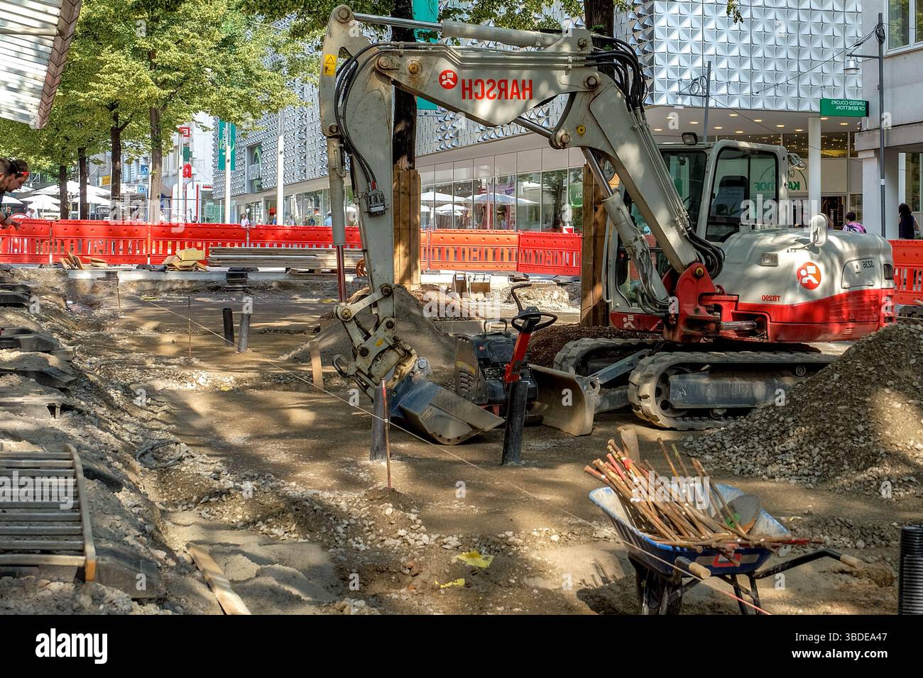 The image shows a construction site next to a row of shops. The area is ...