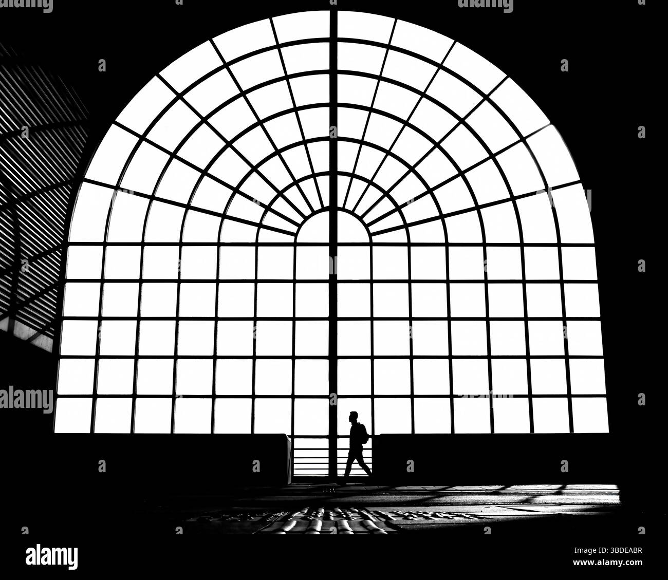 A big backlit window and the silhuette of a man walking in balack and ...