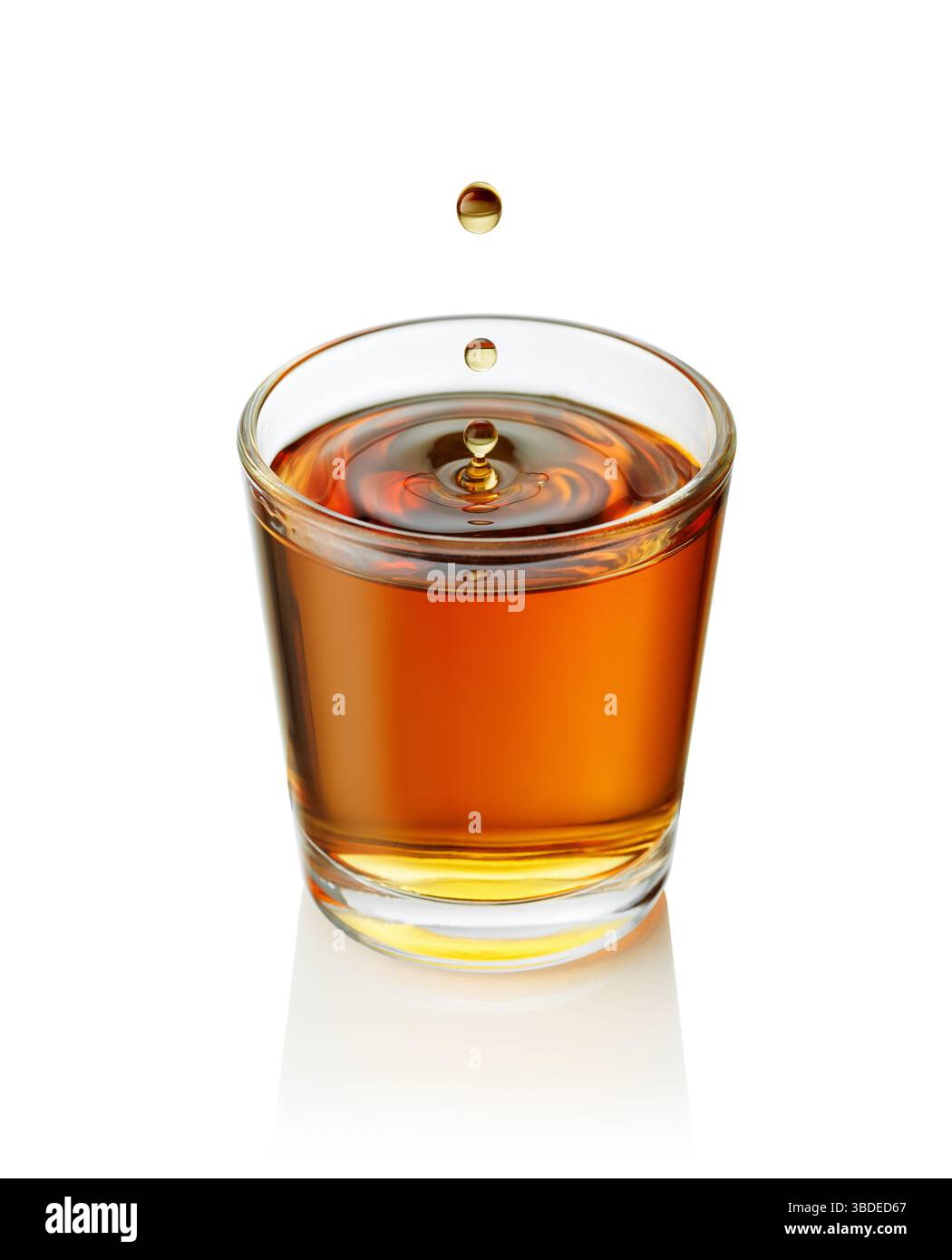 Golden drop splashing into glass whisky or tequila, creating ...