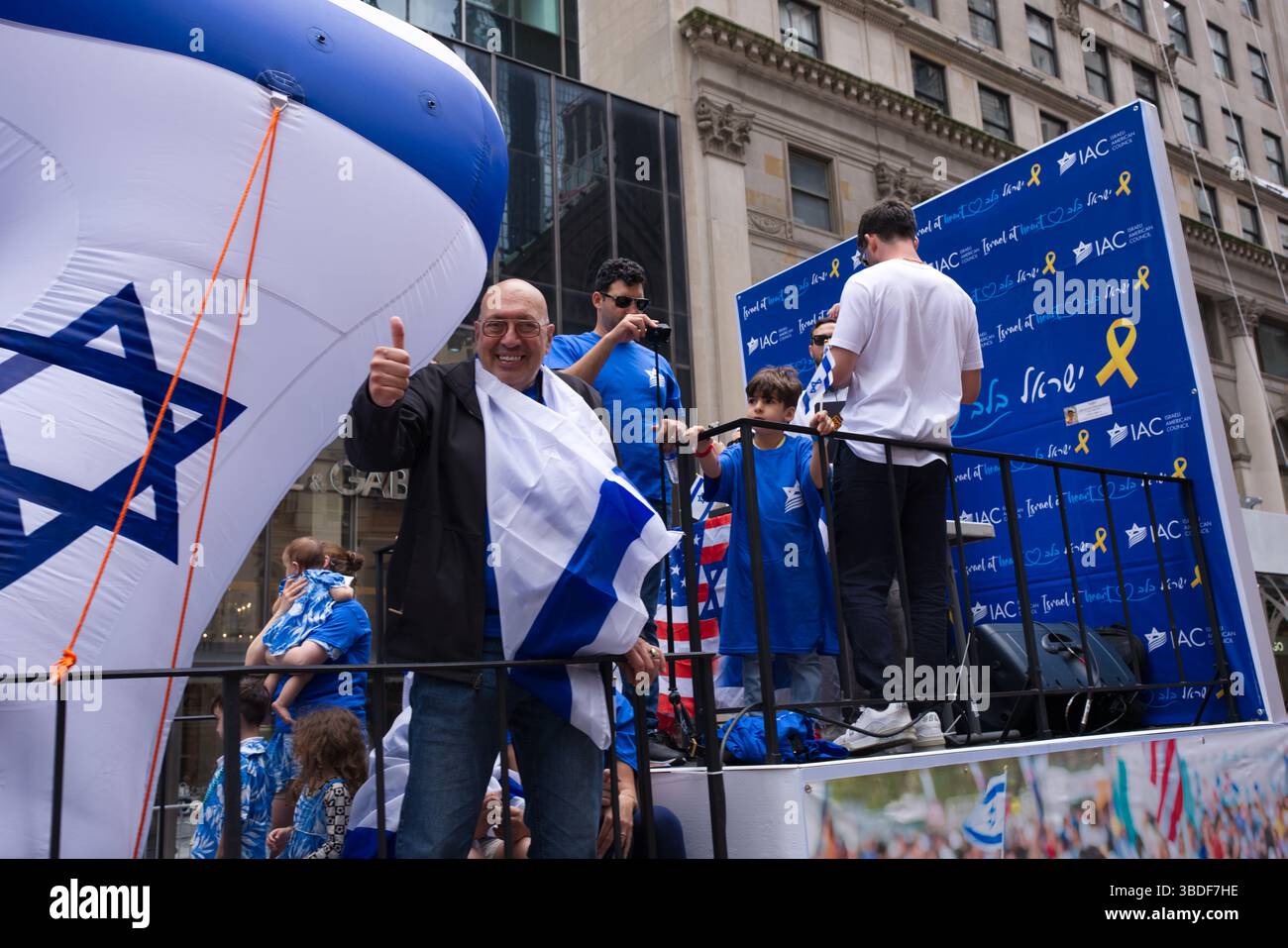 A man gives a thumbs-up, draped in an Israeli flag, standing on a float ...