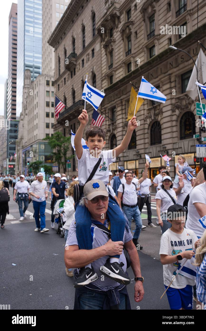 A man carries a boy on his shoulders during a parade. The boy holds two ...