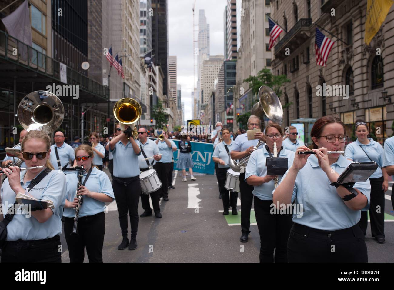A marching band in light blue uniforms parades down a city street ...
