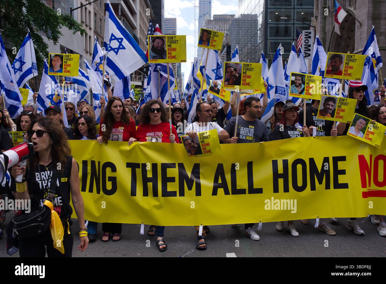 A large group of protestors march down a city street, holding signs ...