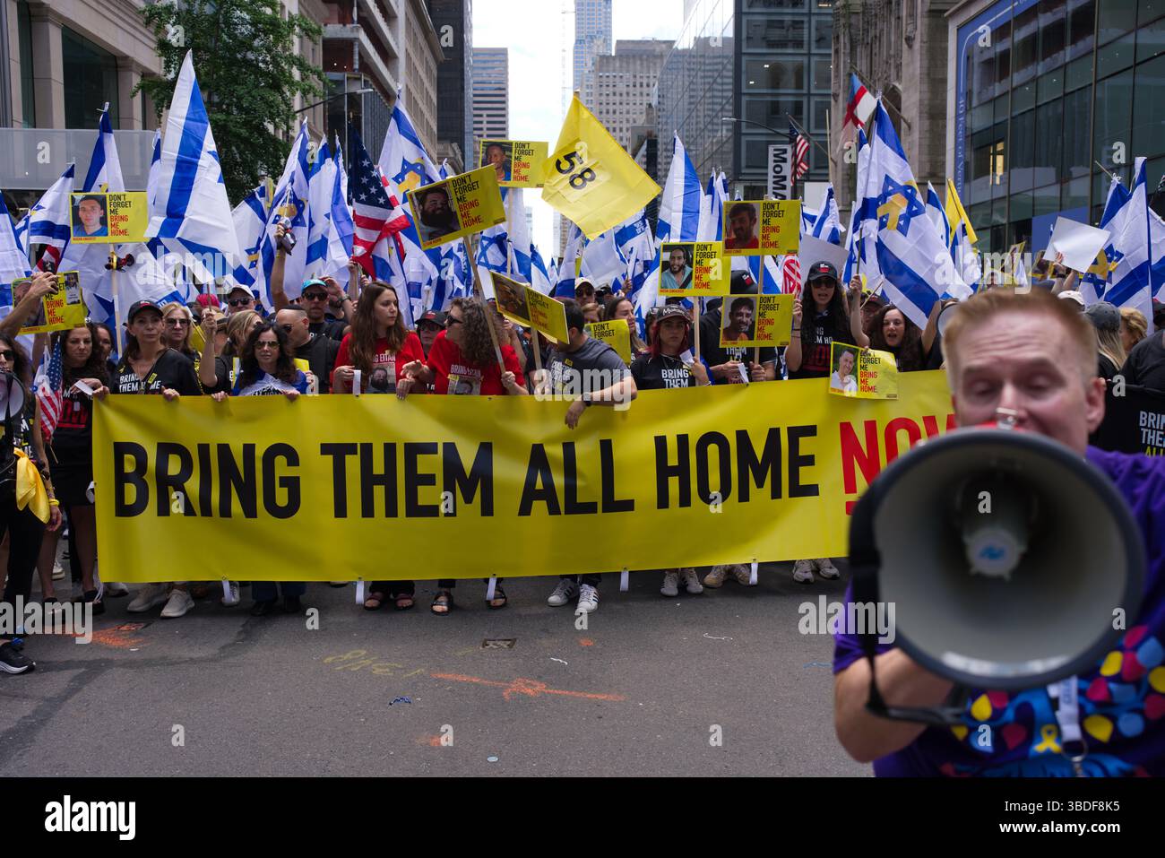 A large group of protestors hold signs and a banner reading "Bring Them ...