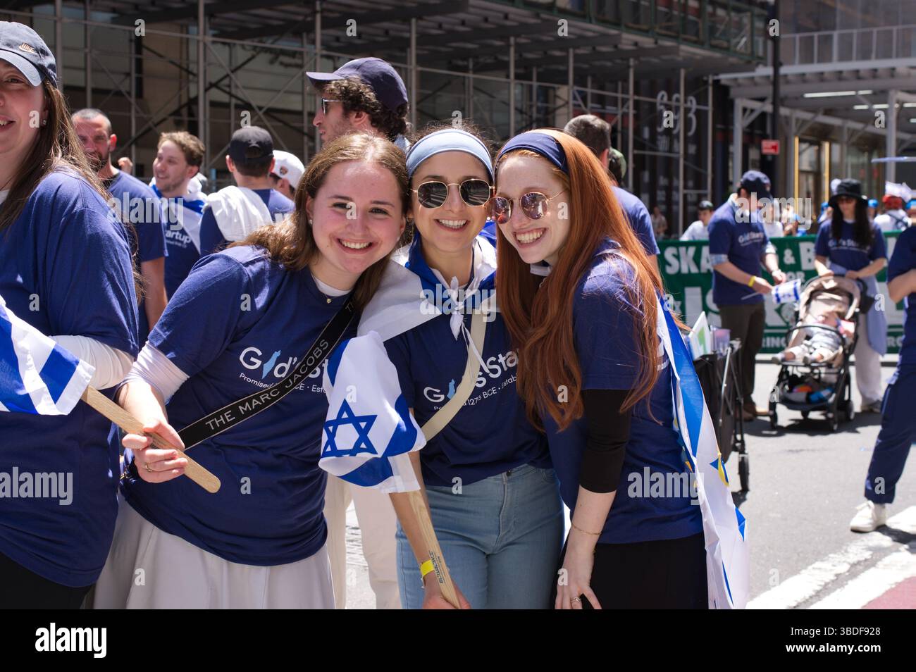 Three young women, smiling, hold Israeli flags at a parade. They wear ...