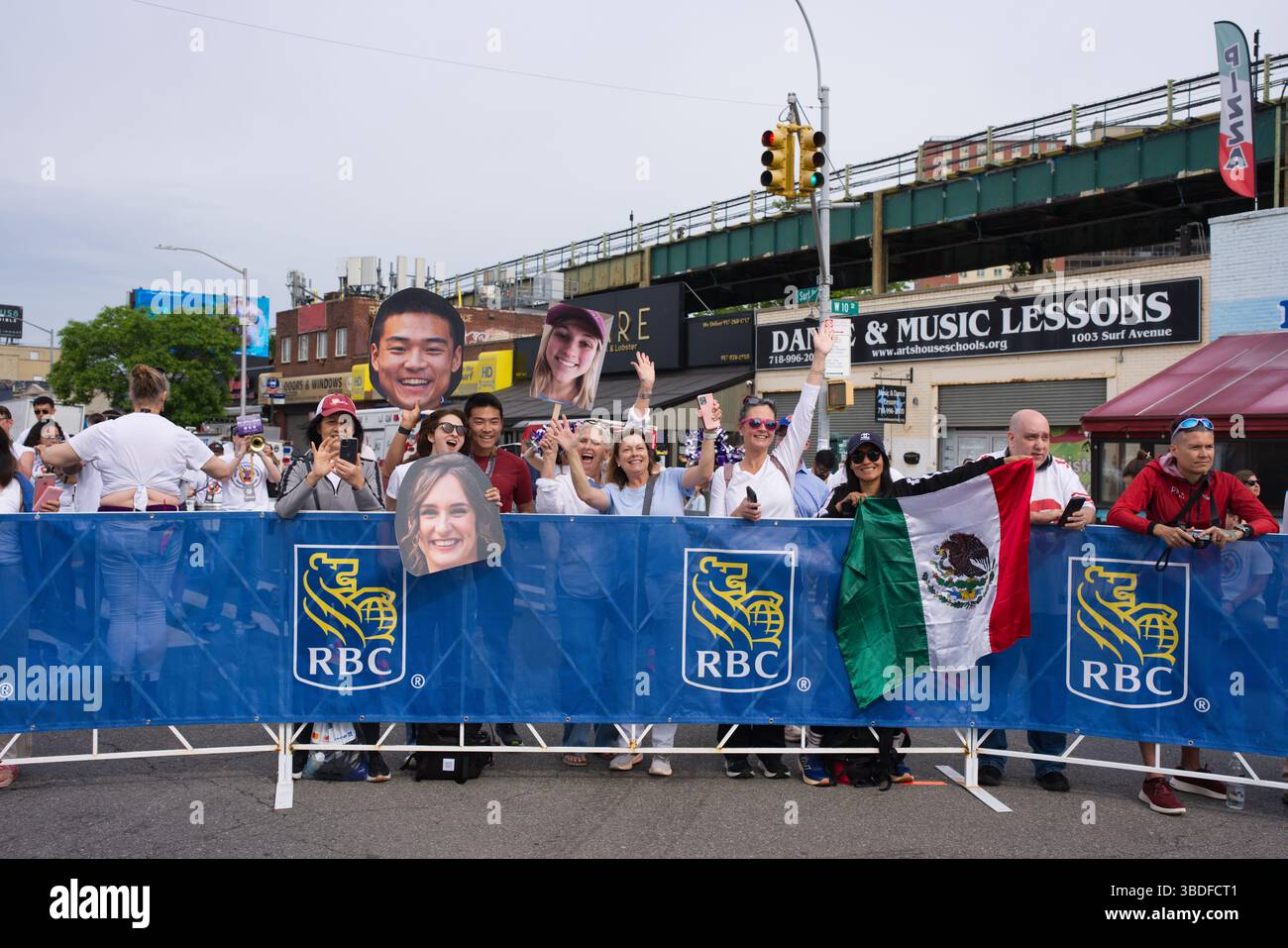 A crowd of spectators, many holding large photos of faces, stand behind ...