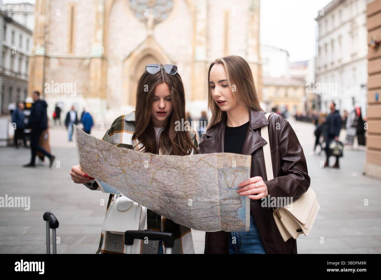Two female tourists standing with luggage while reading a map and ...