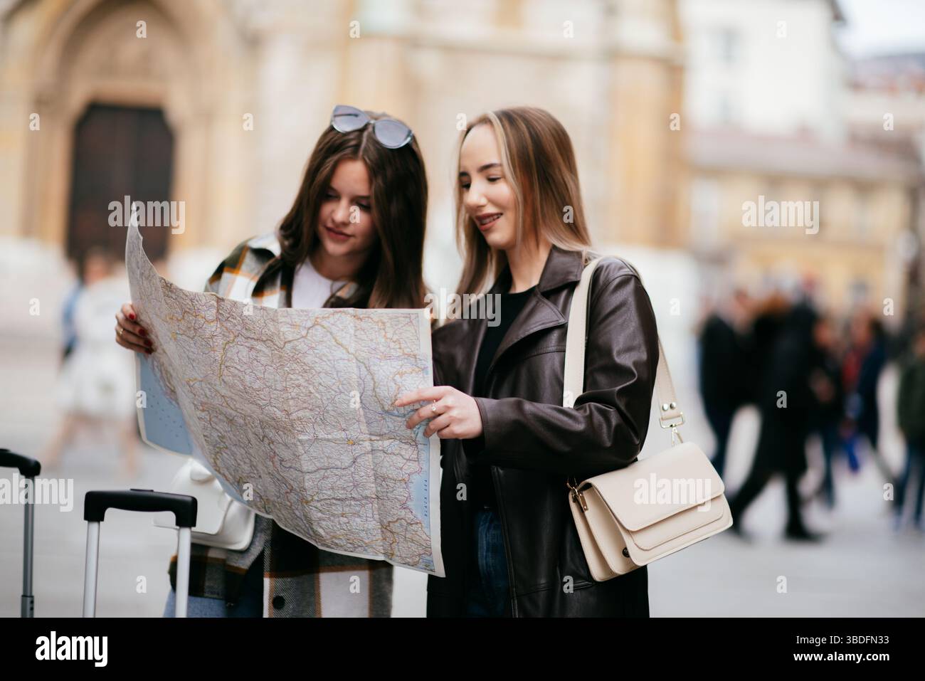 Two female tourists standing with luggage while reading a map and ...